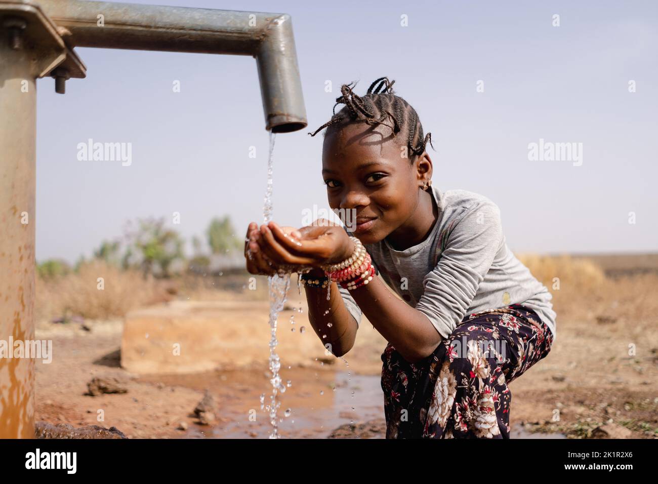 Smiling african girl tasting fresh water flowing from a tap in the ...
