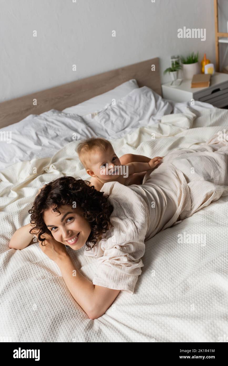 high angle view of infant baby lying near cheerful and curly mother in ...