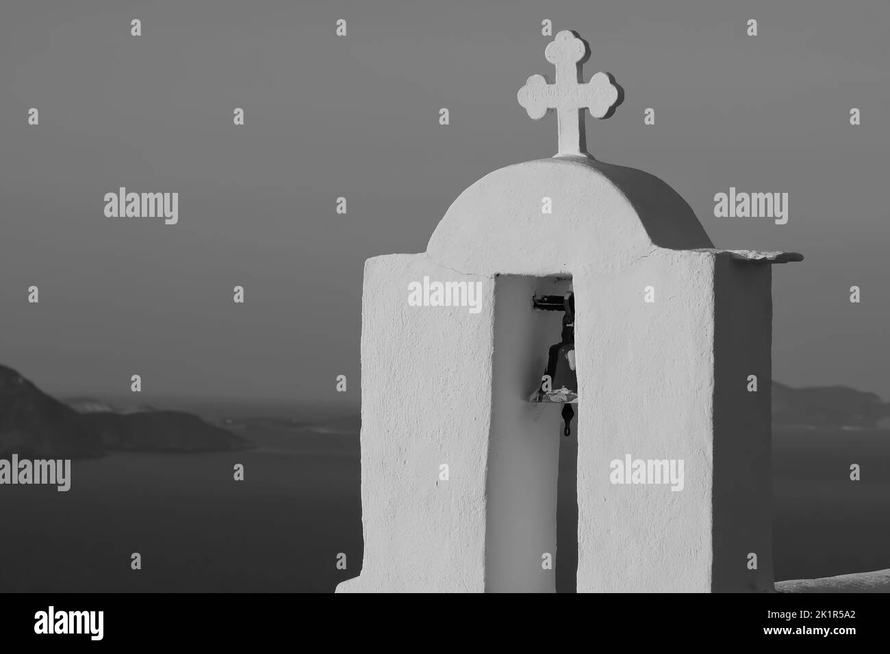 A cross and a bell on the top of an orthodox church in Ios Greece while ...