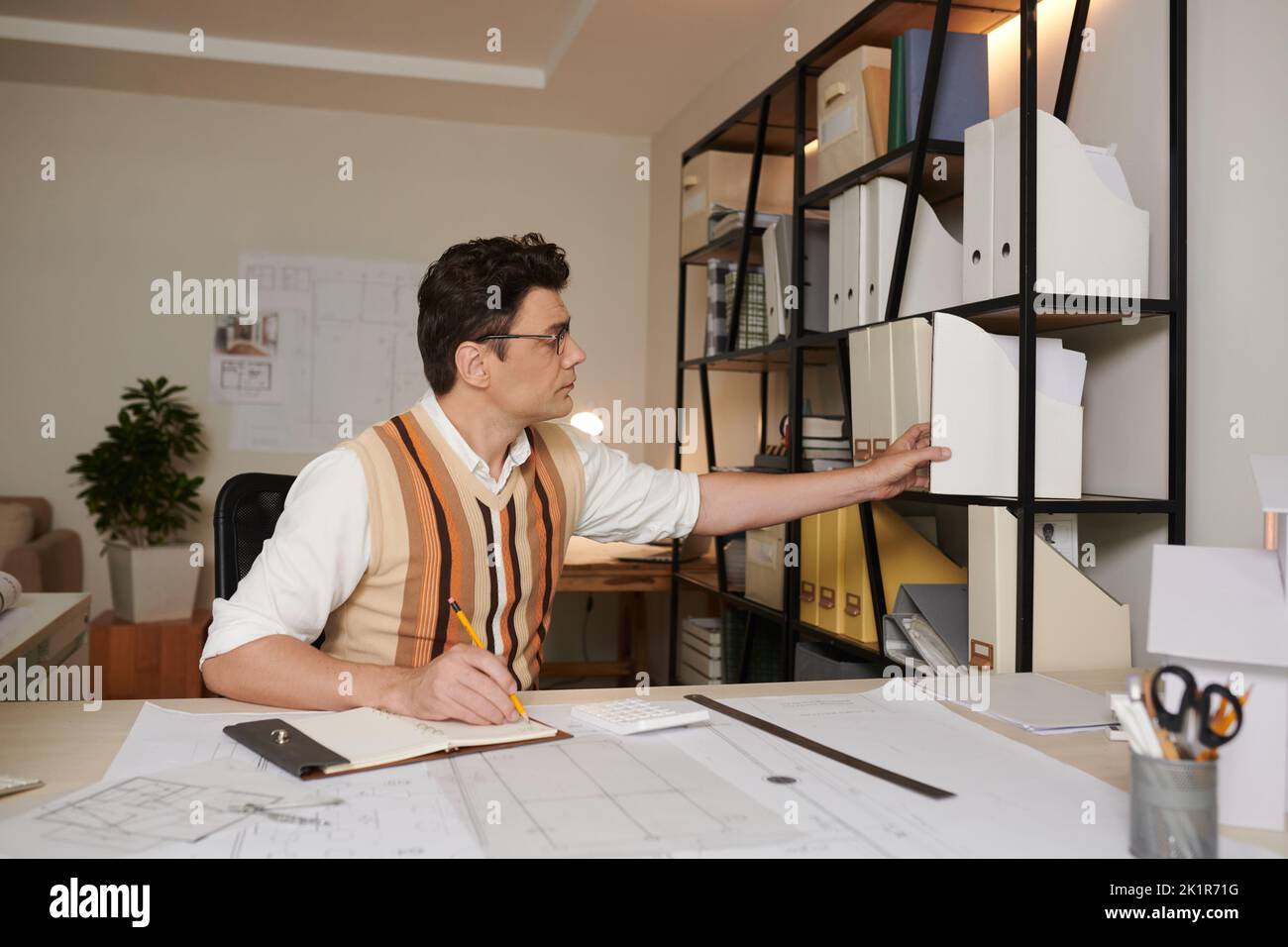 Engineer taking folder with technical documentation fron self in office ...