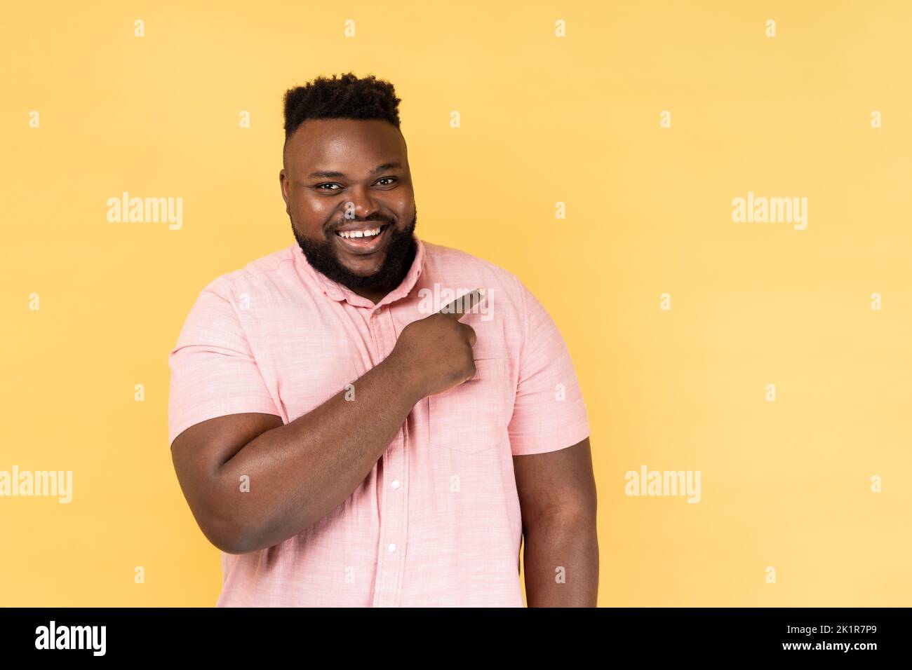 Portrait of man wearing pink shirt pointing aside, showing blank copy ...