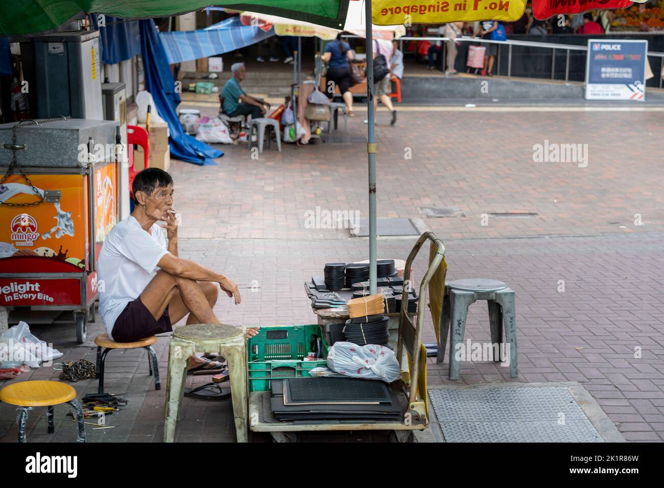 Street vendor smoking a cigarette while sitting under umbrella on ...