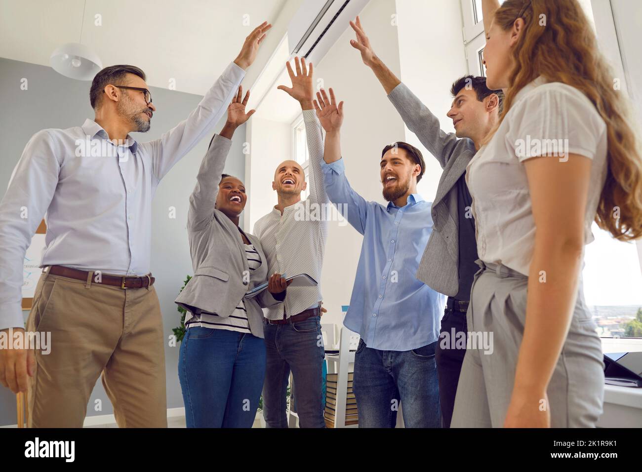 Positive motivated colleagues raise their hands together symbolizing ...