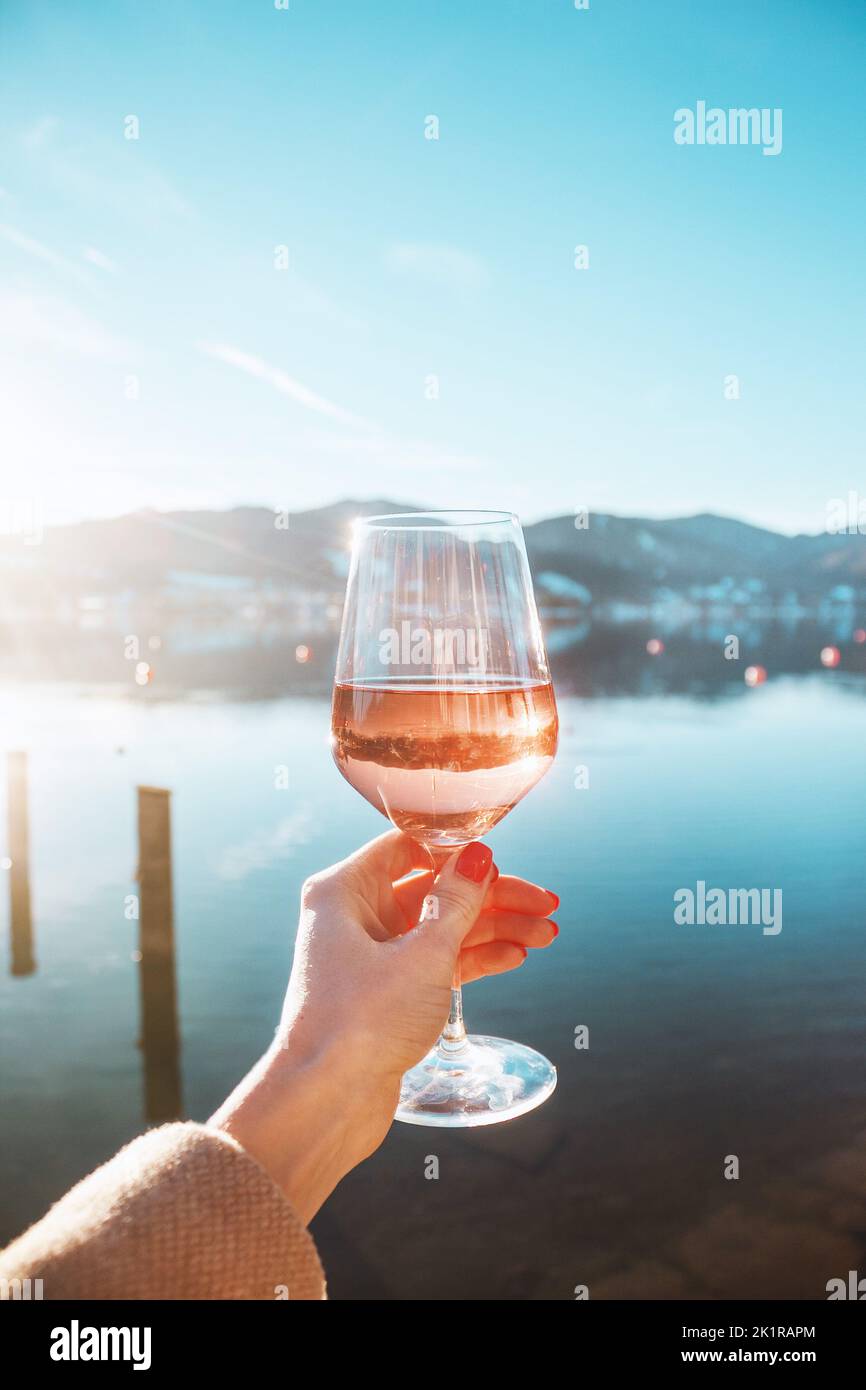 Female hand with glass of rose wine. Cozy pier on the coast of the lake ...