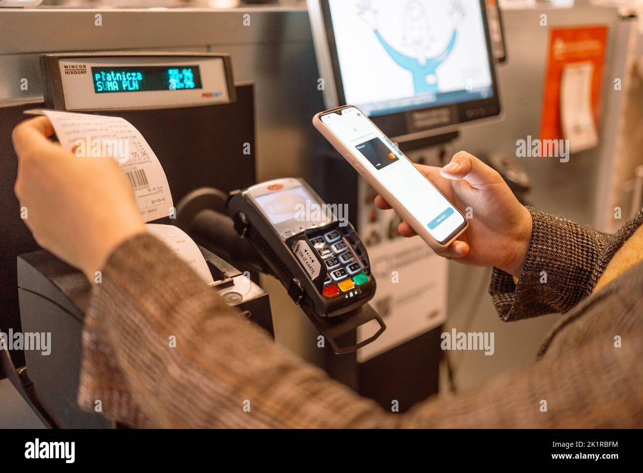 Side view of young woman paying at self-checkout using smartphone app ...