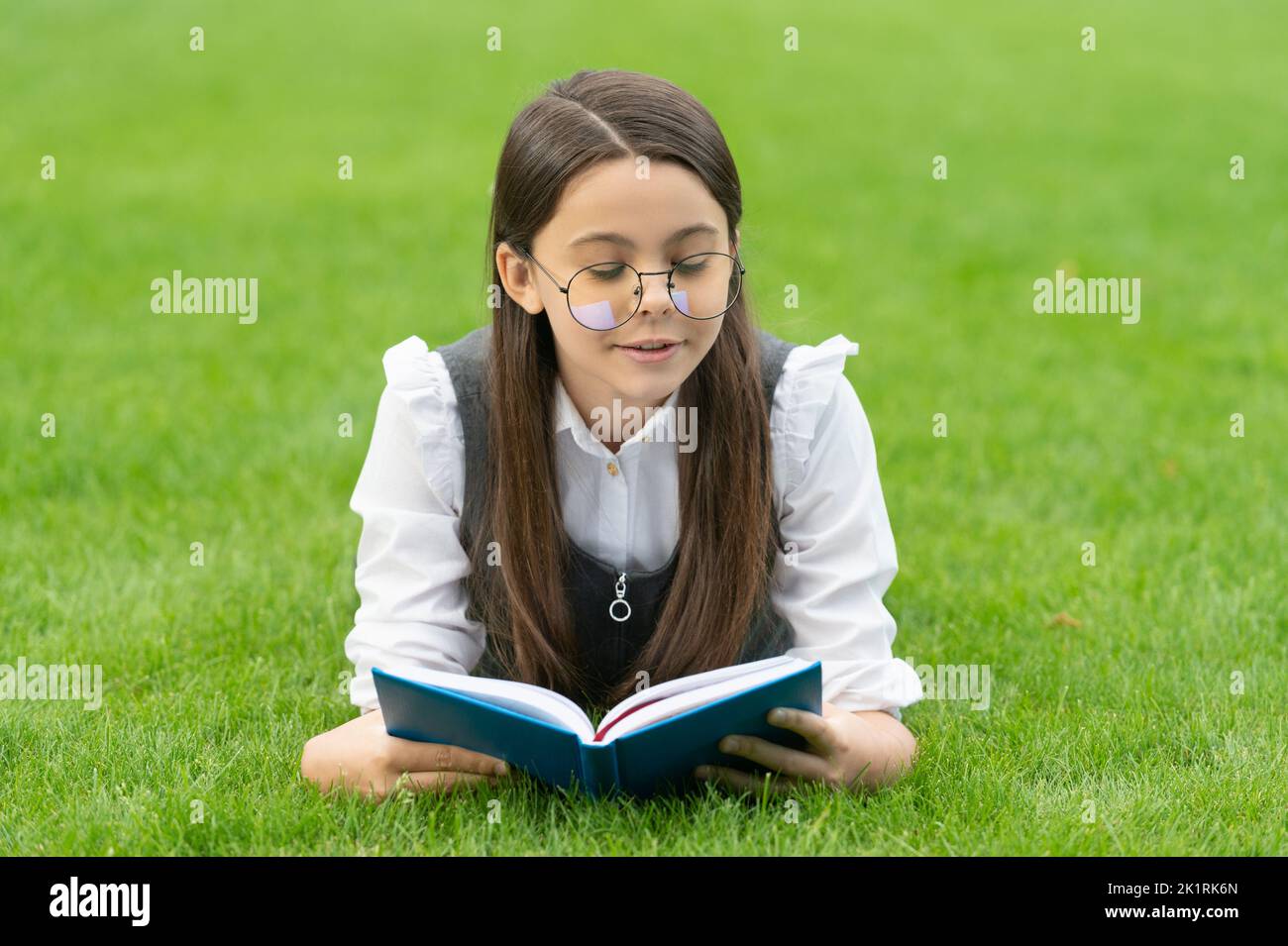 Serious schoolgirl reading book lying on grass, reading. Teen ...