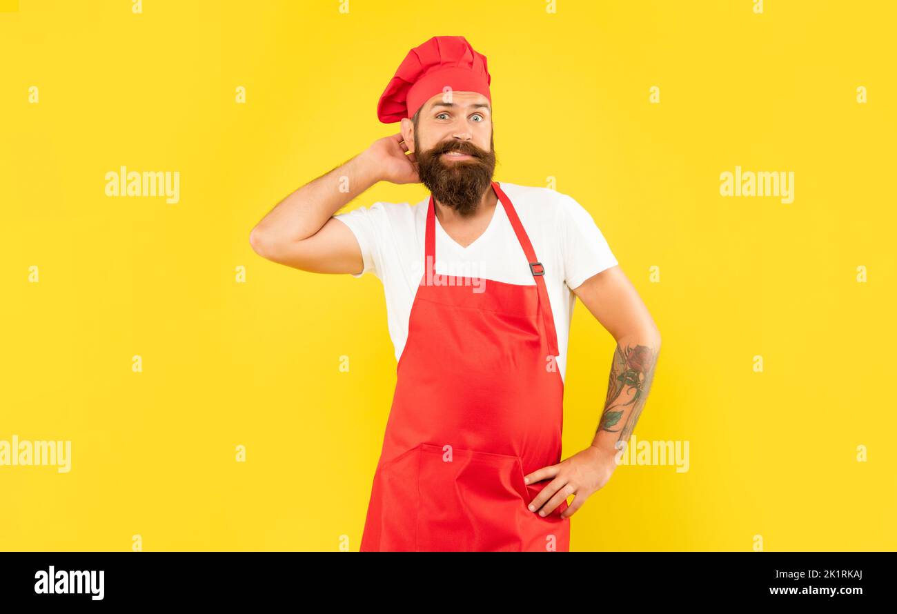 Hesitant man in red toque and apron scratching head yellow background ...