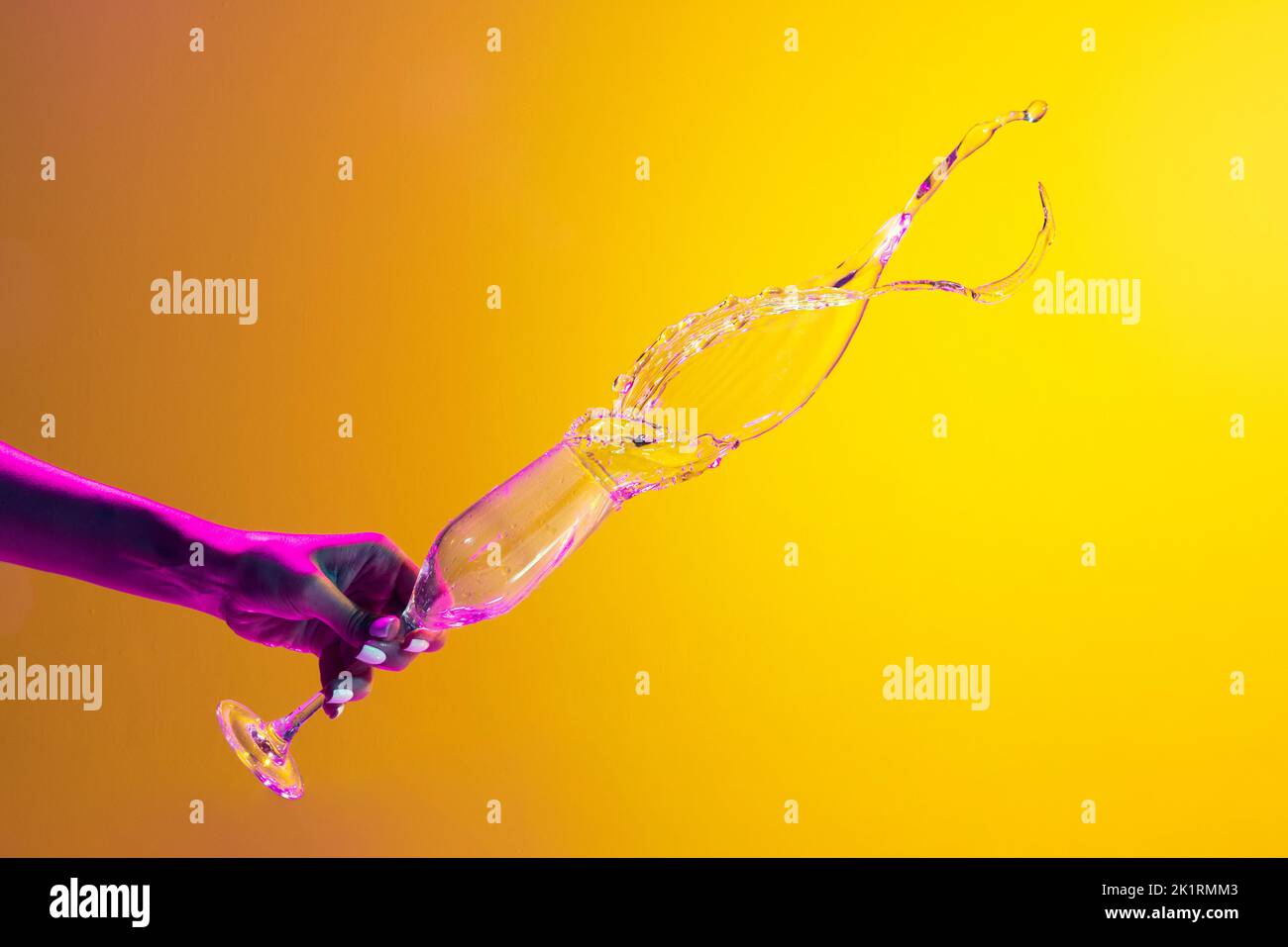 Female hand spilling over champagne isolated over yellow background in ...