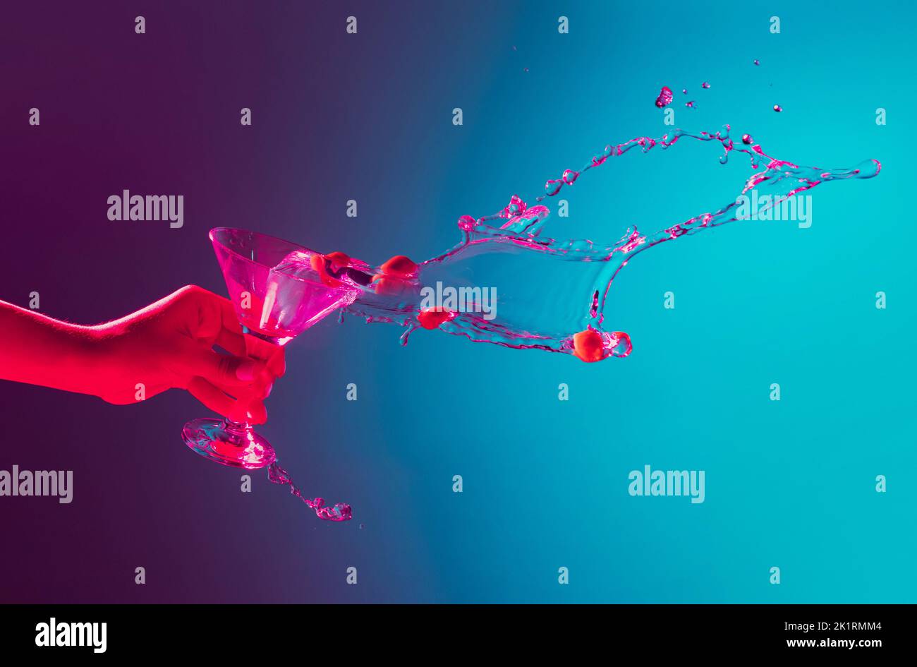 Female hand spilling over Martini cocktail splash over blue background ...