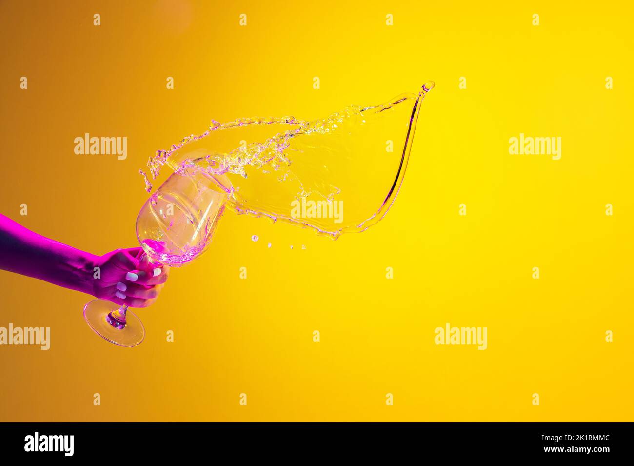 Female hand spilling over champagne isolated over yellow background in ...