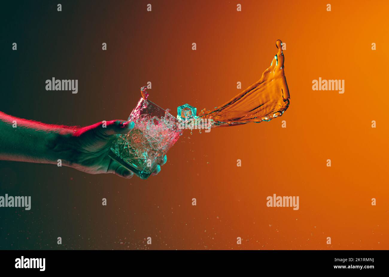 Male hand spilling over whiskey, splashes over blue dark orange ...