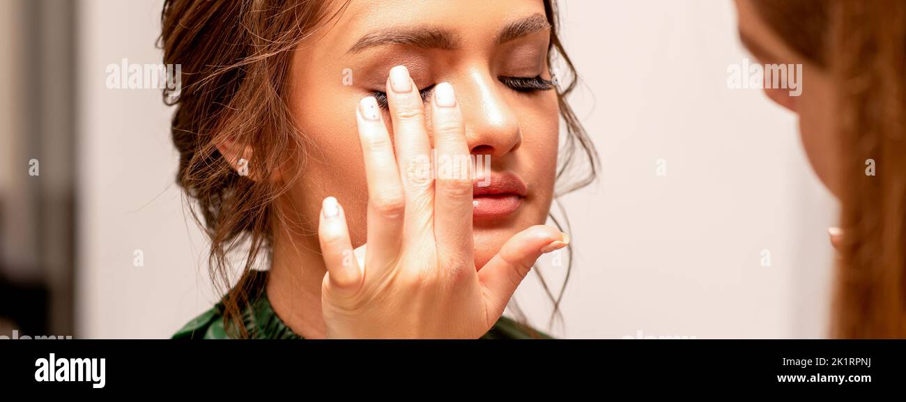 The hand of a makeup artist applies eye shadow on the eyelid of a young ...