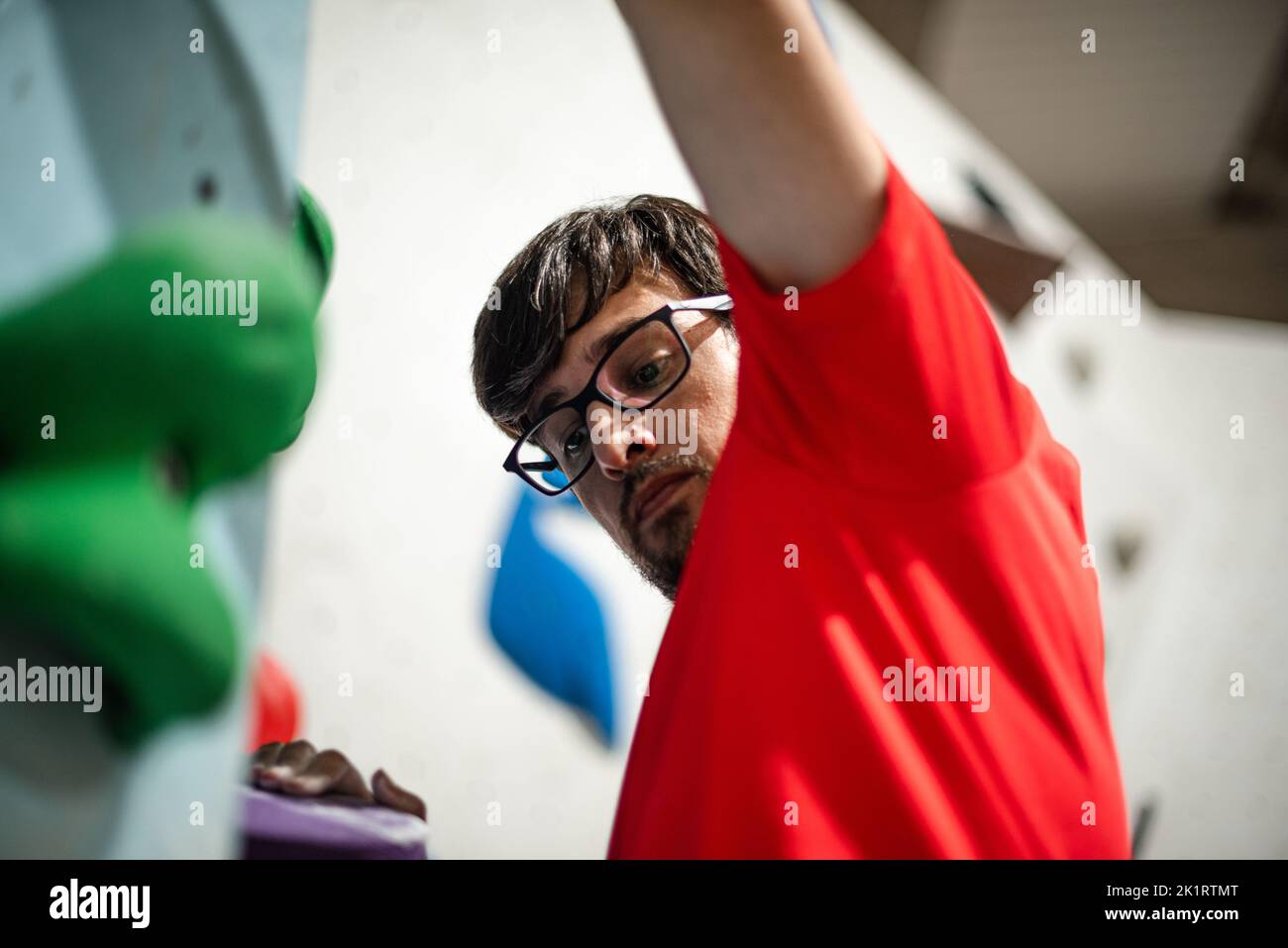 Man stretching his arm to reach a climbing hold on a climbing wall ...