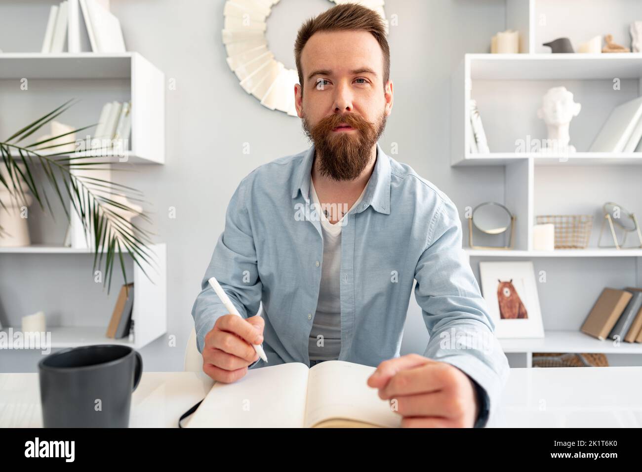 Young bearded man sitting at the desk and taking notes at home Stock ...