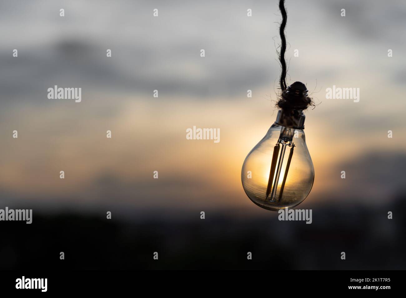 Light bulb hanging by a rope illuminated by the sunset sun with a city ...