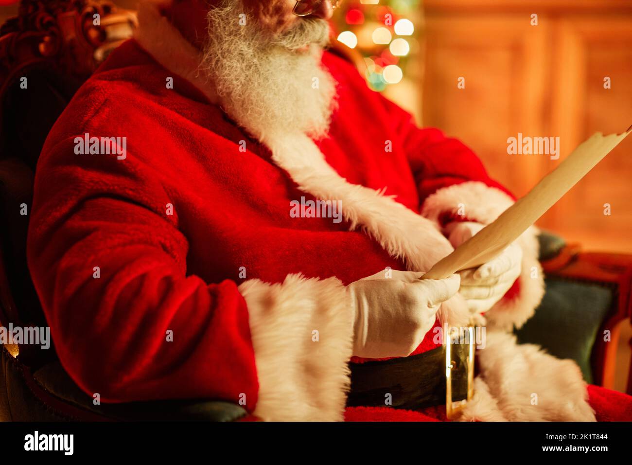 Side view of traditional Santa Claus reading letter by fireplace on ...