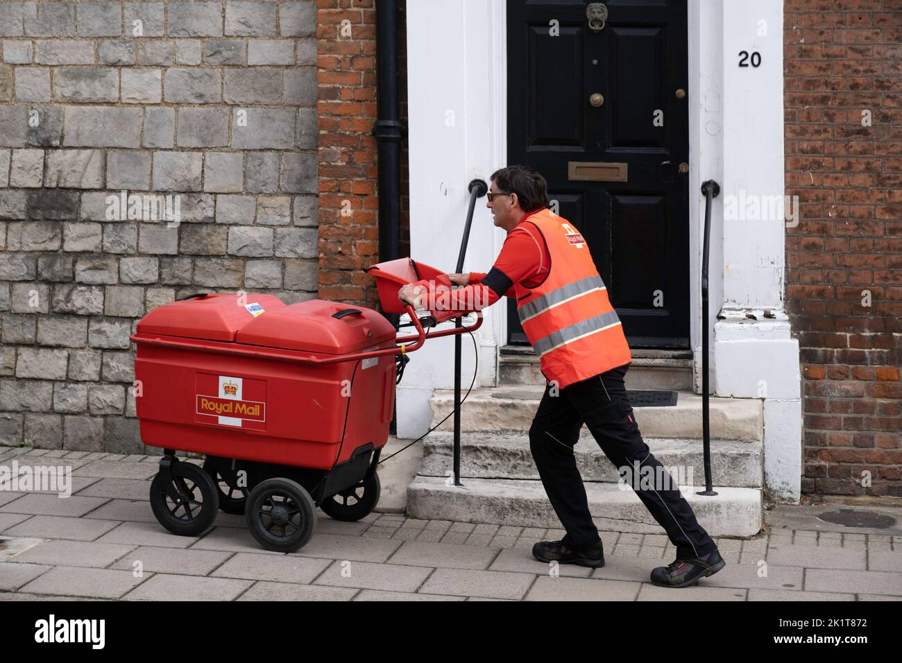 Postman in orange jacket employed by England's Royal Mail pushes a ...