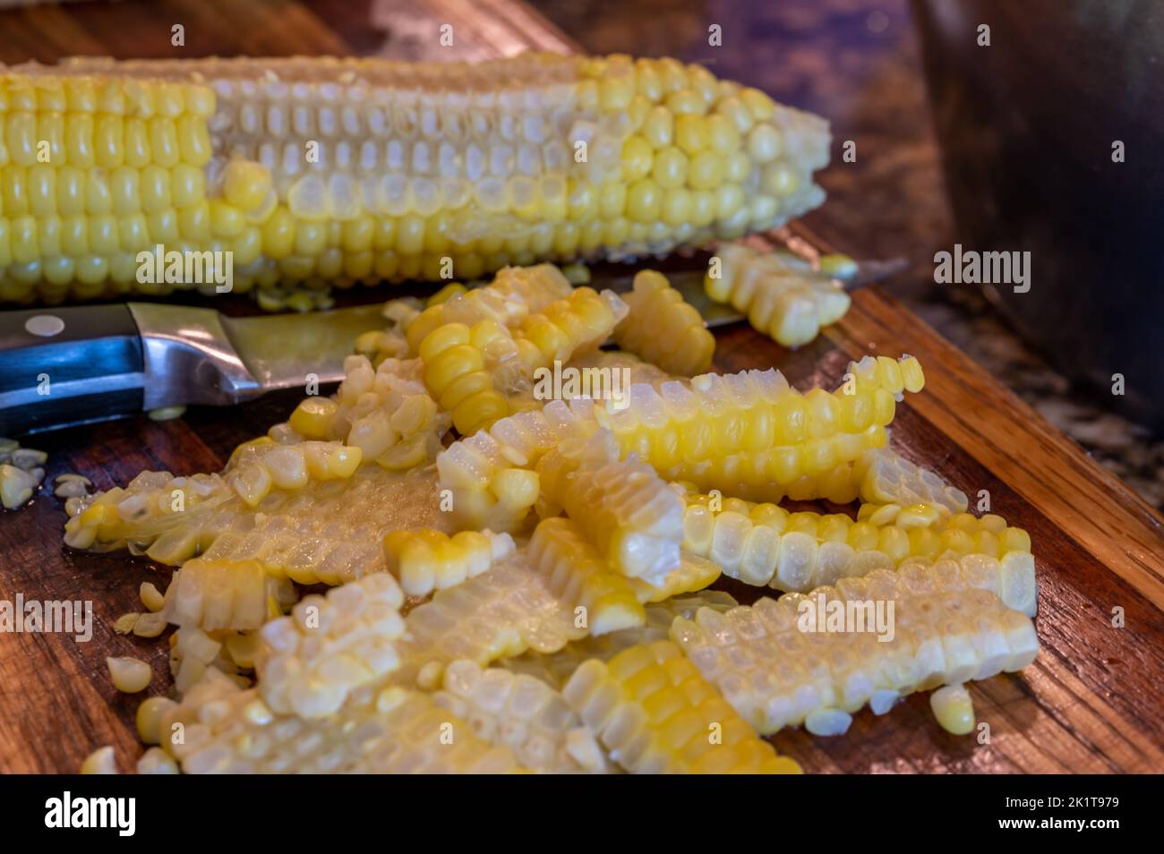 Using a knife to remove kernels from the cob of an ear of sweet corn ...