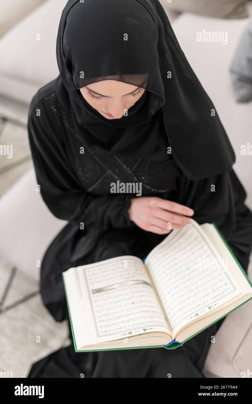 Young traditional muslim woman reading Quran on the sofa before iftar ...