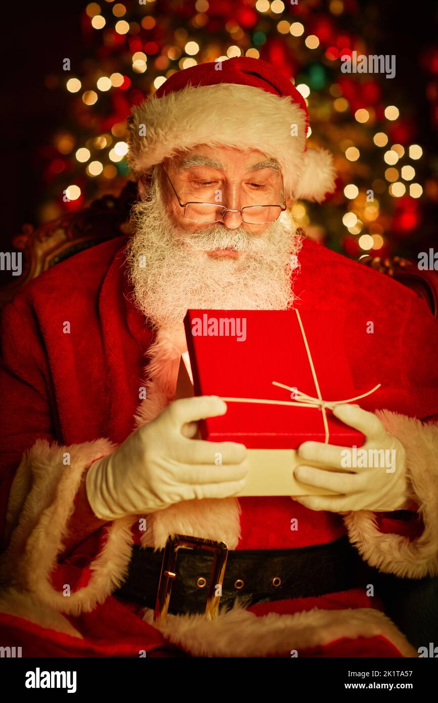 Vertical portrait of bearded traditional Santa Claus opening present ...