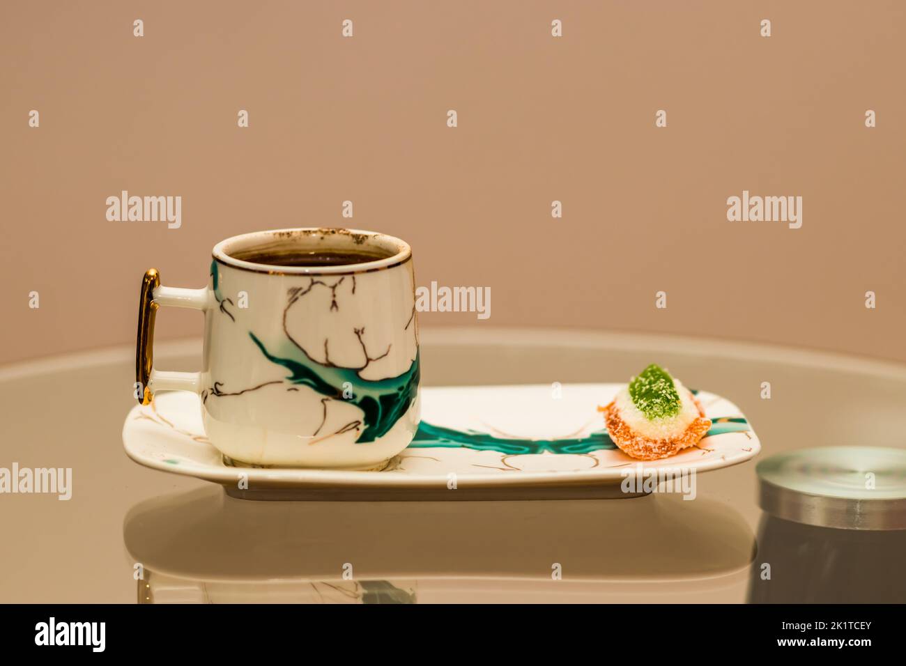 A cup of coffee and a dessert on a white plate on a glass table Stock ...