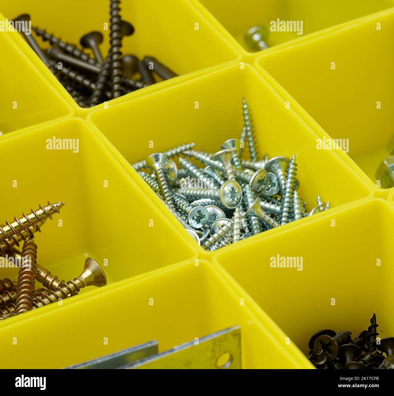 Various metal screws in separate yellow plastic containers. The concept ...