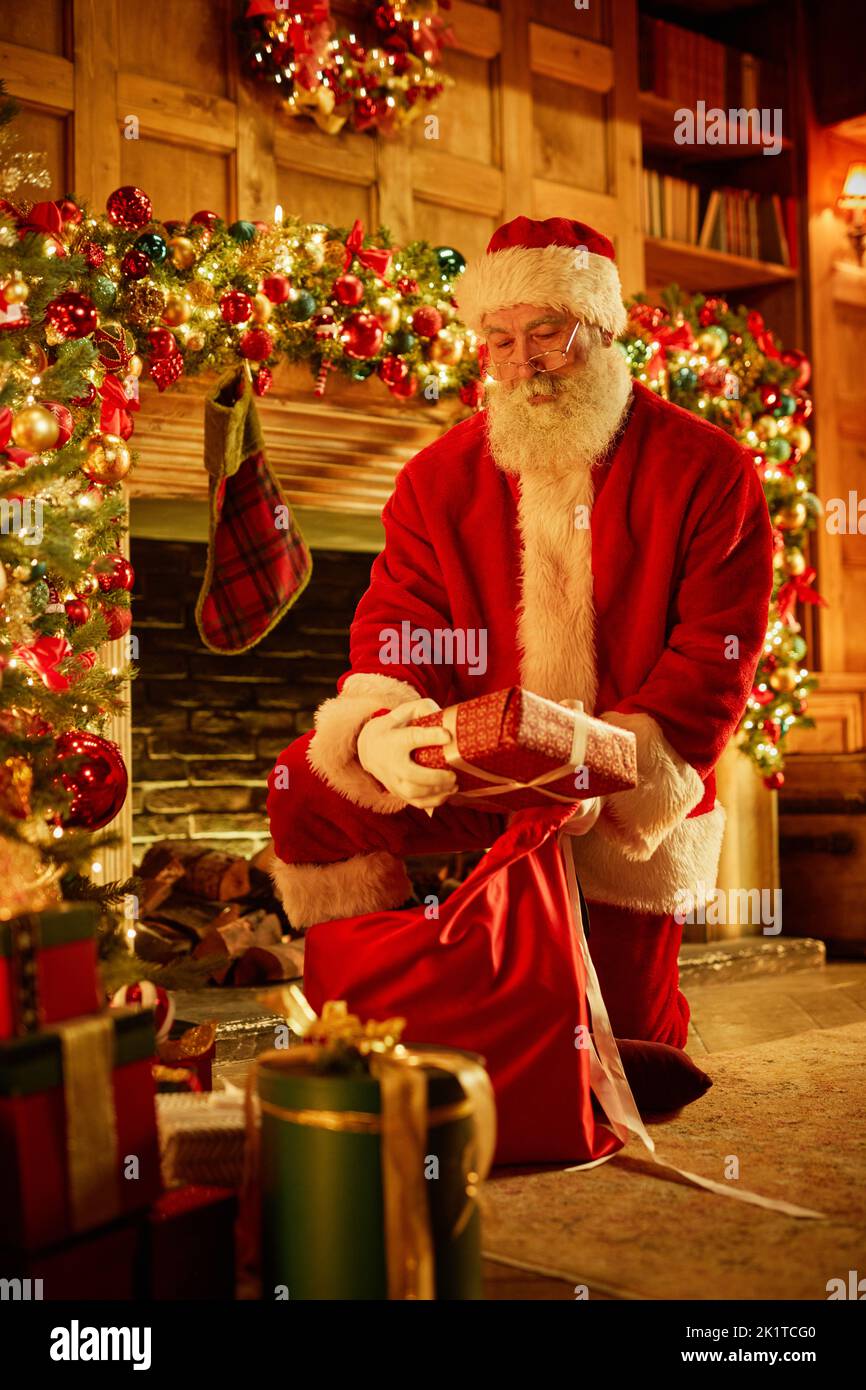 Vertical portrait of Santa Claus putting presents under Christmas tree ...