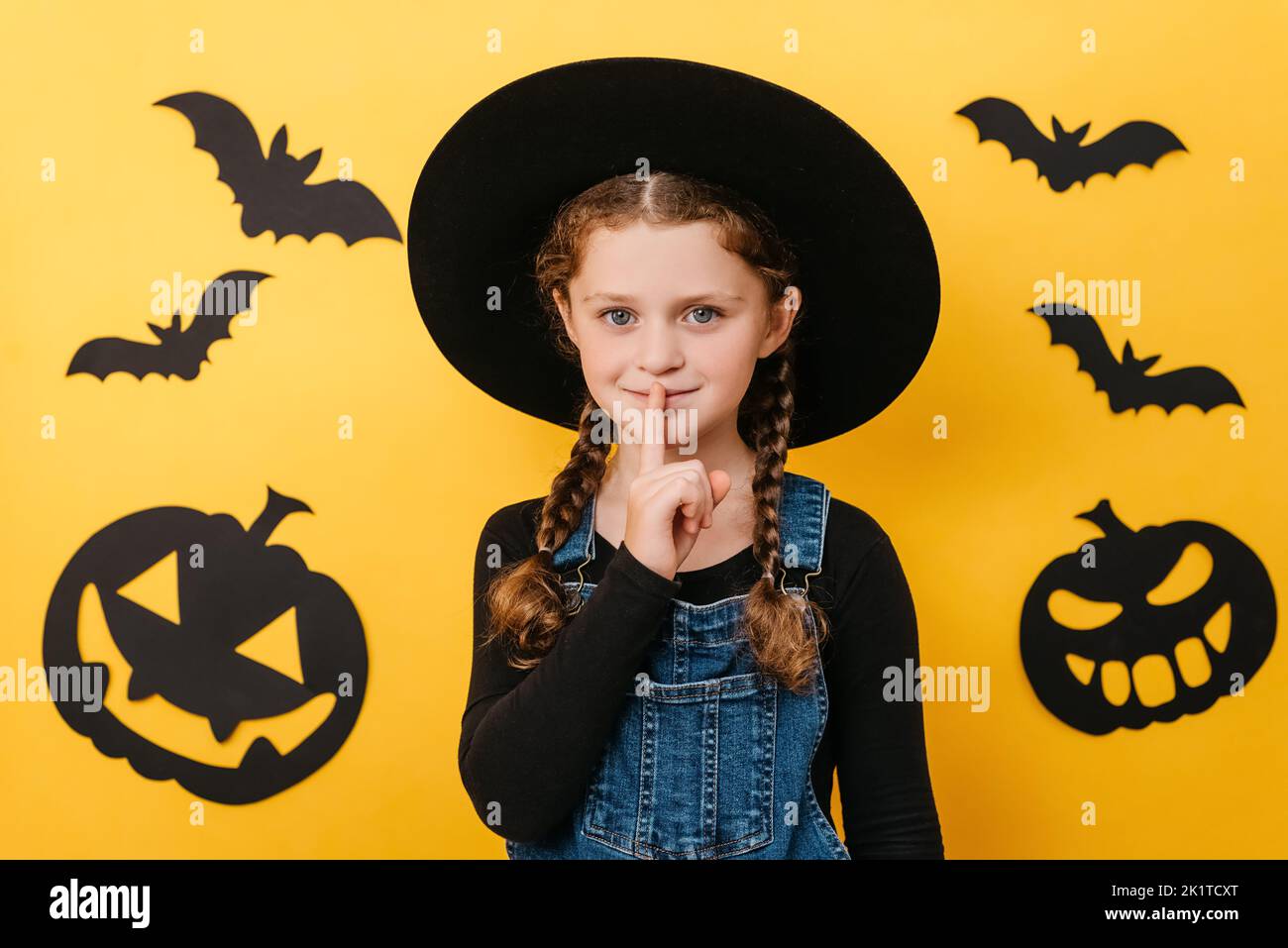 Portrait of secret little girl child in big black hat say hush be quiet ...