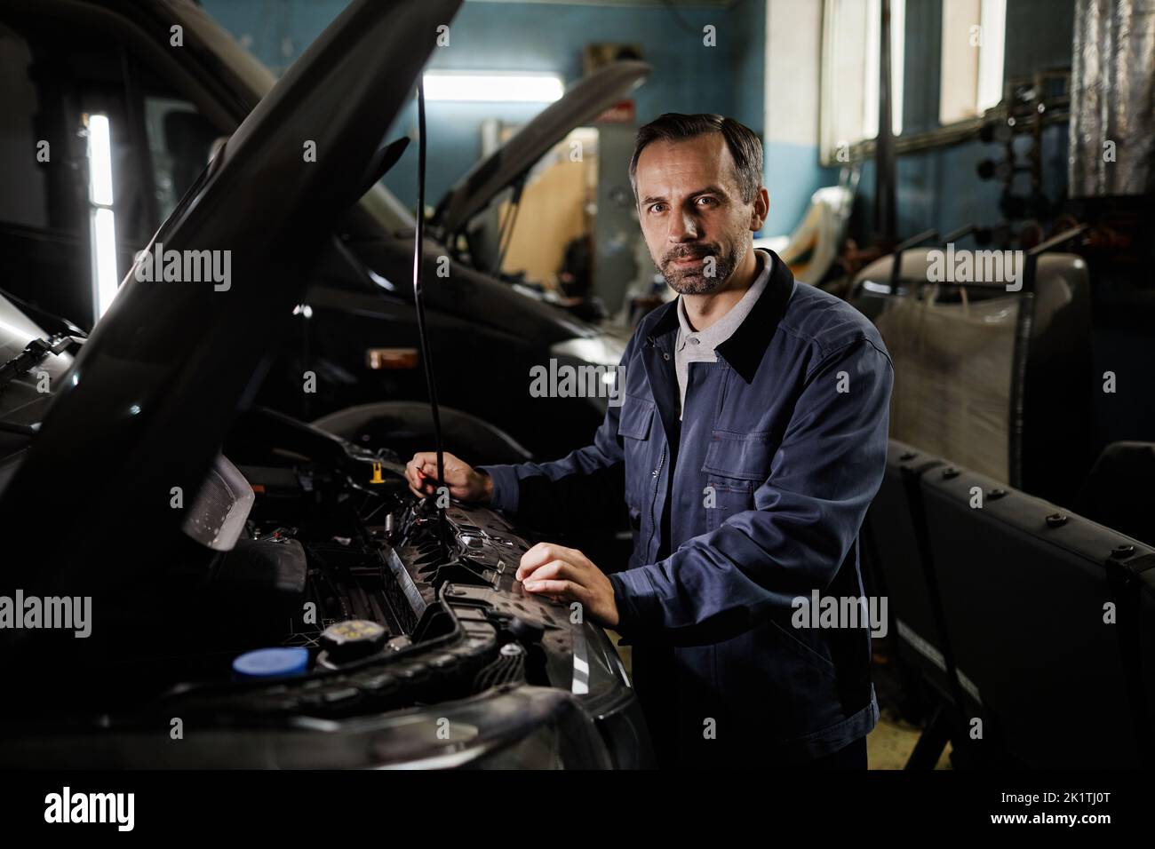 Waist up portrait of mature car mechanic repairing trucks in garage and ...