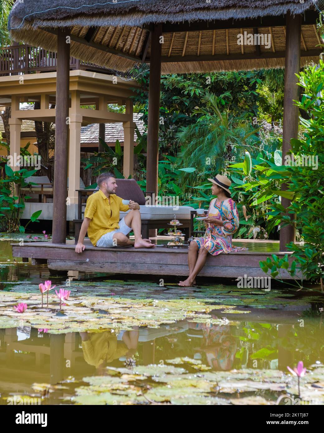 Afternoon tea at a water pond, high tea in a tropical garden in Thailand. Couple of men and ...