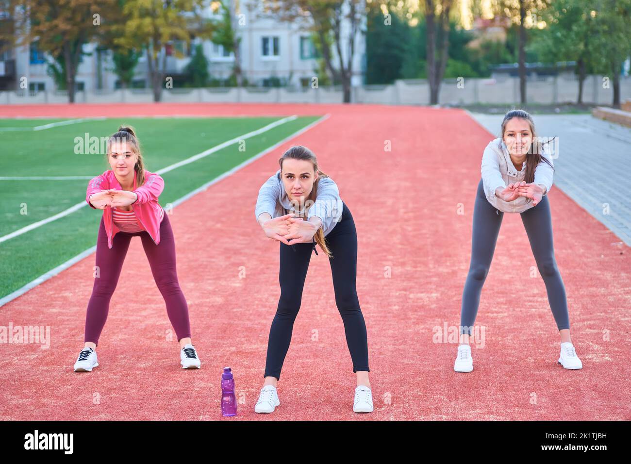 Three girls doing stretching exercises at the football stadium Stock ...