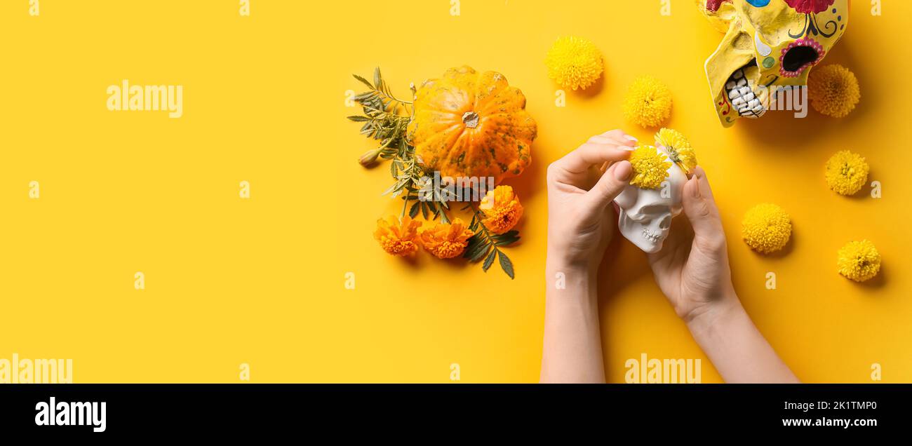 Hands with human skulls, flowers and pumpkin on yellow background ...