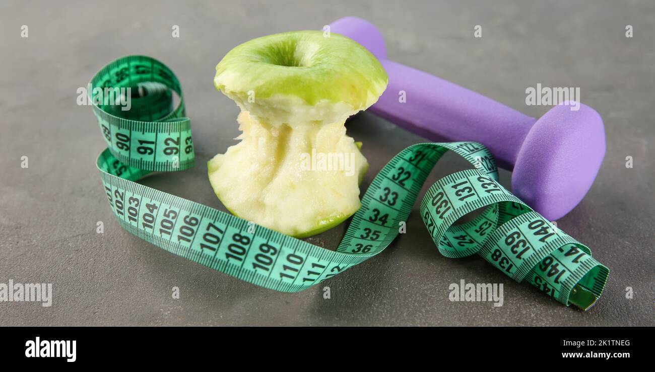 Bitten apple, dumbbell and measuring tape on grey background. Diet ...