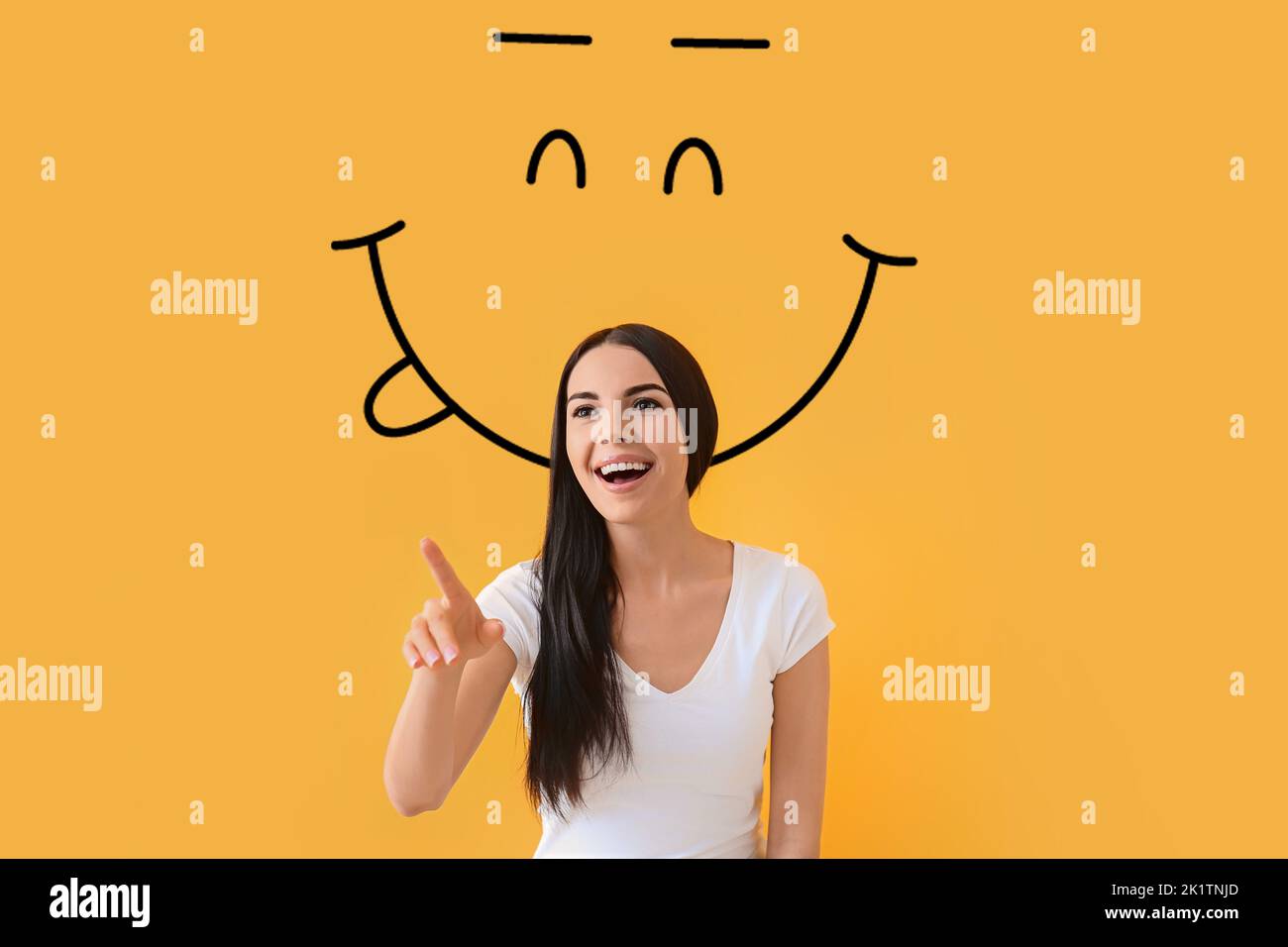 Beautiful young woman pointing at something and drawn smile on yellow ...