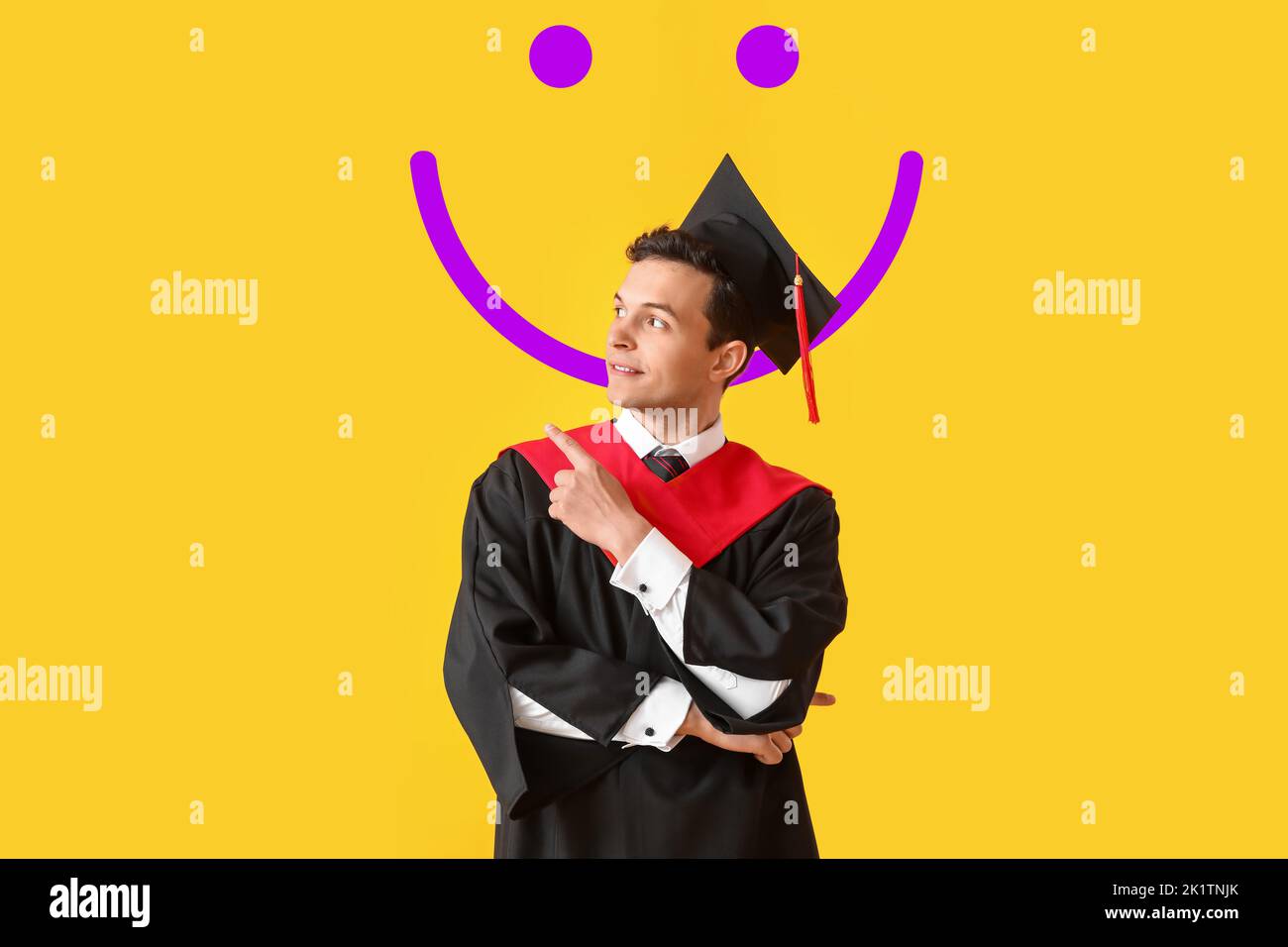 Male graduating student pointing at something and drawn smile on yellow ...