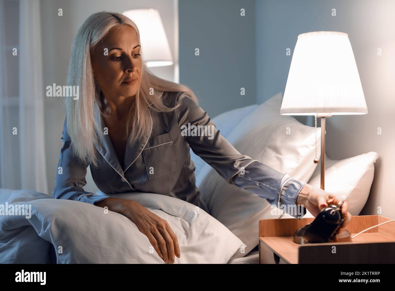 Stressed mature woman with alarm clock sitting on bed at night Stock ...