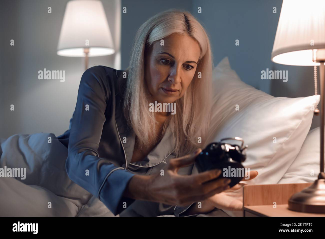 Stressed mature woman with alarm clock lying in bed at night Stock ...
