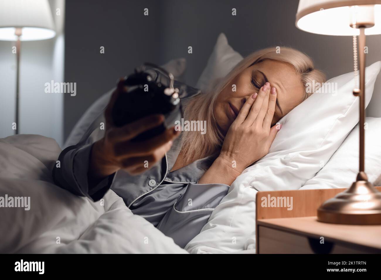 Stressed mature woman with alarm clock lying in bed at night Stock ...