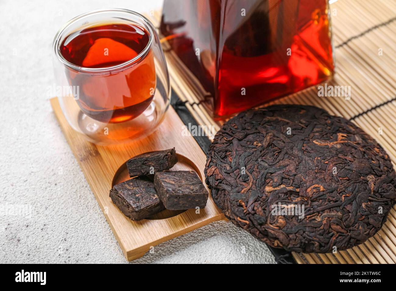 Board with dry pressed puer tea and glass on white background, closeup ...