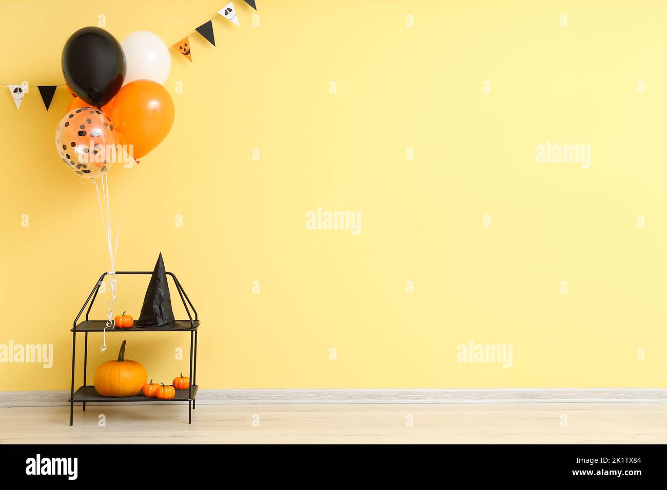 Table with Halloween pumpkins, witch hat, balloons and flags on yellow ...