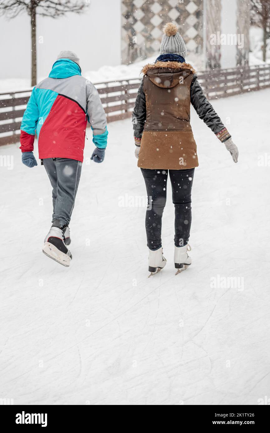 Two abstract young people, girl and guy skating on rink in city park ...