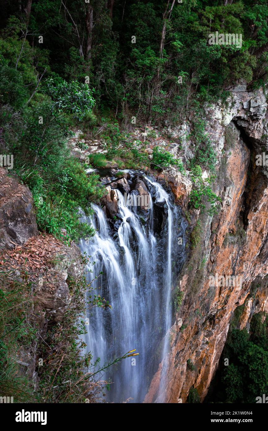 A powerful waterfall surrounded by lush green trees and orange rocks in ...