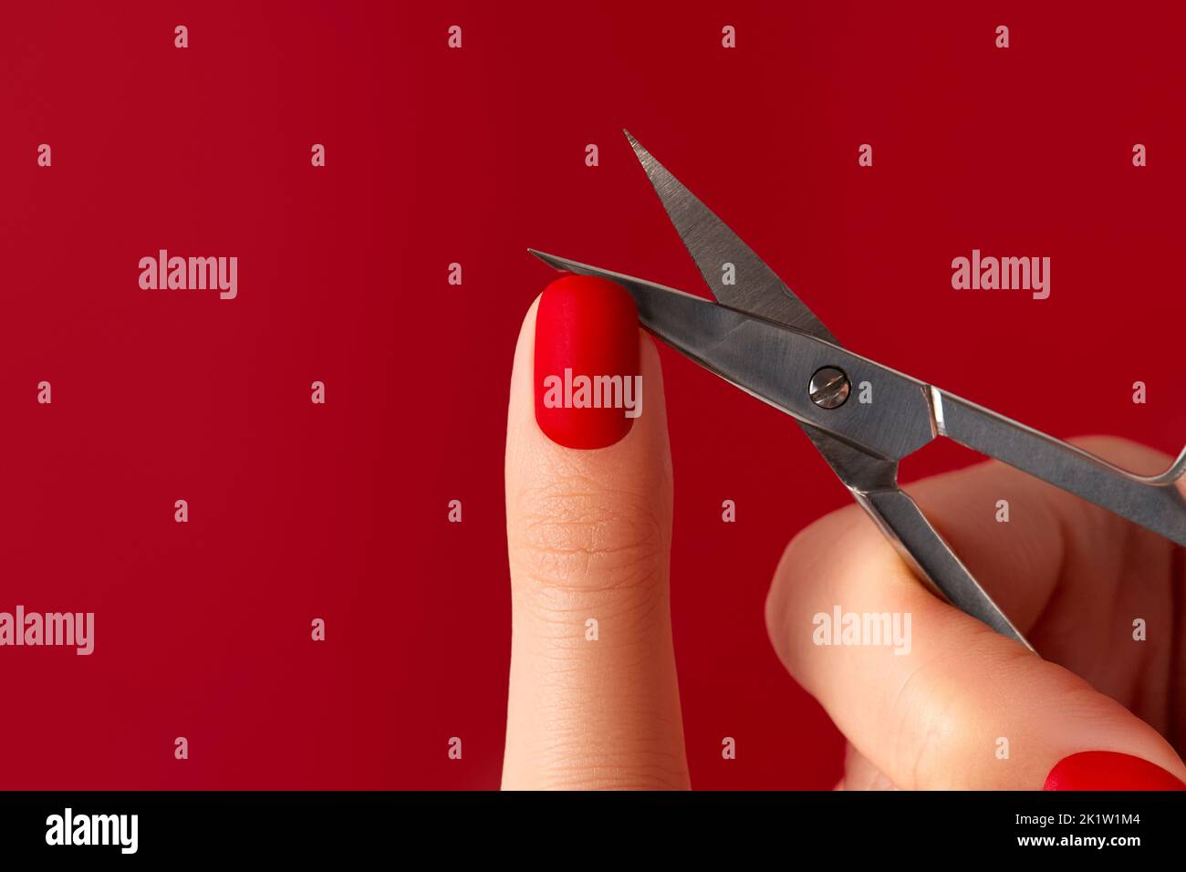 Manicured female hand with scissors on red background. Red matt nail ...
