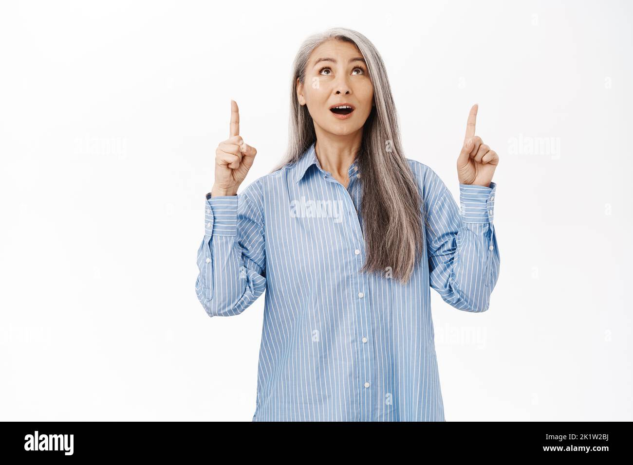 Portrait of excited asian lady, pointing fingers up, looking with ...