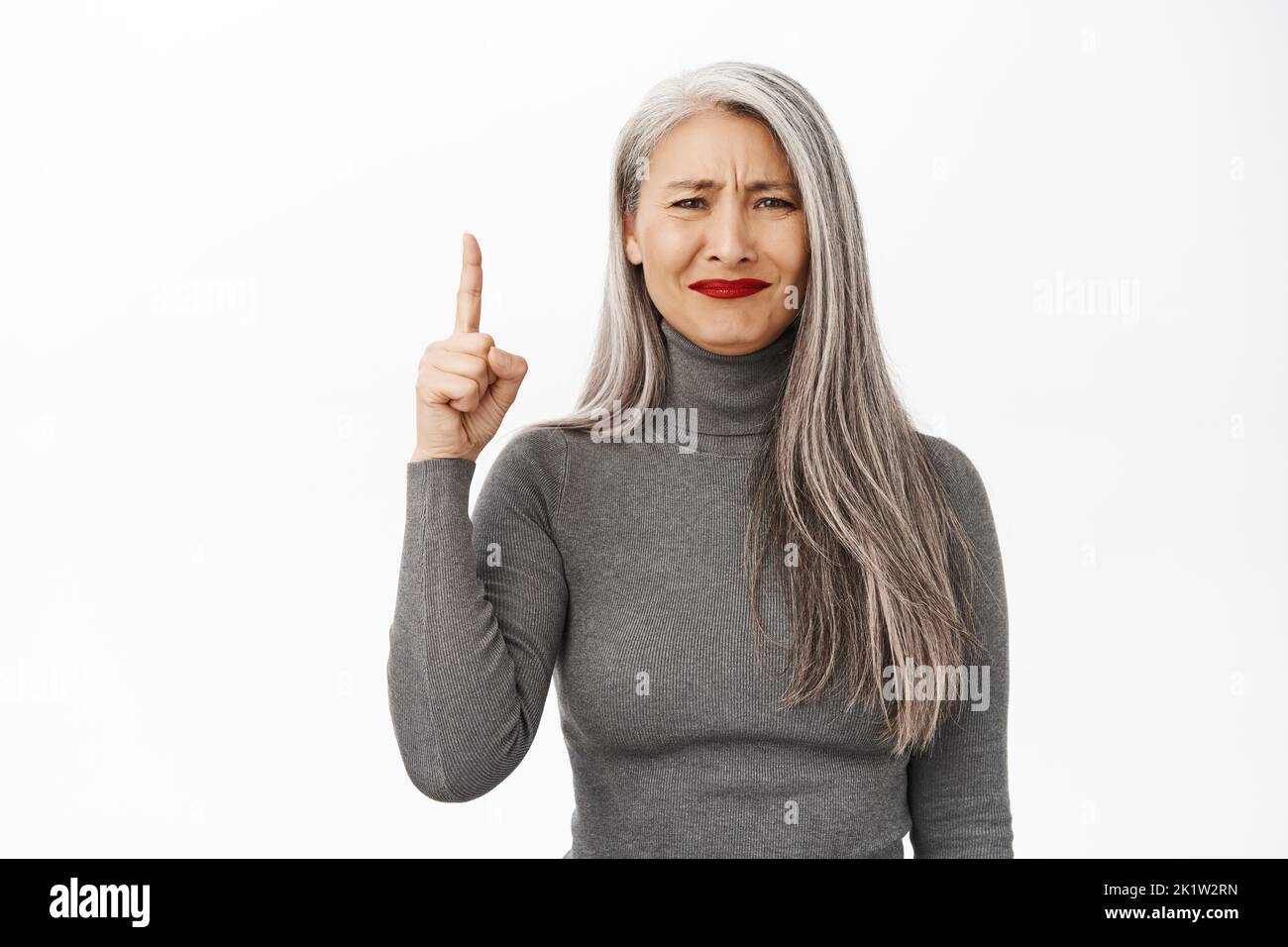 Portrait of disappointed asian woman pointing finger up and grimacing ...