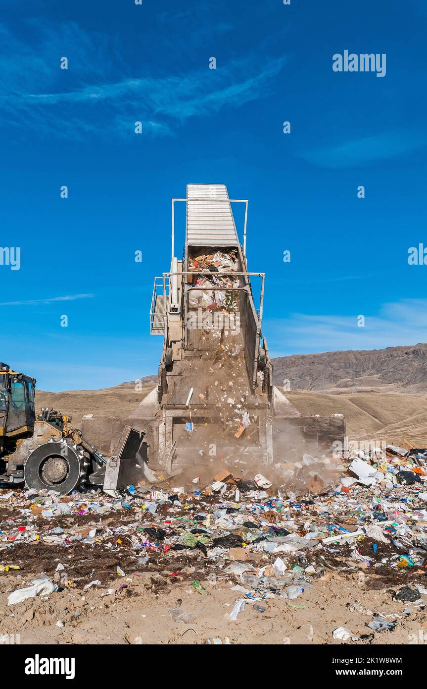 A trailer from a semitrailer truck is in a landfill tipper being raised ...