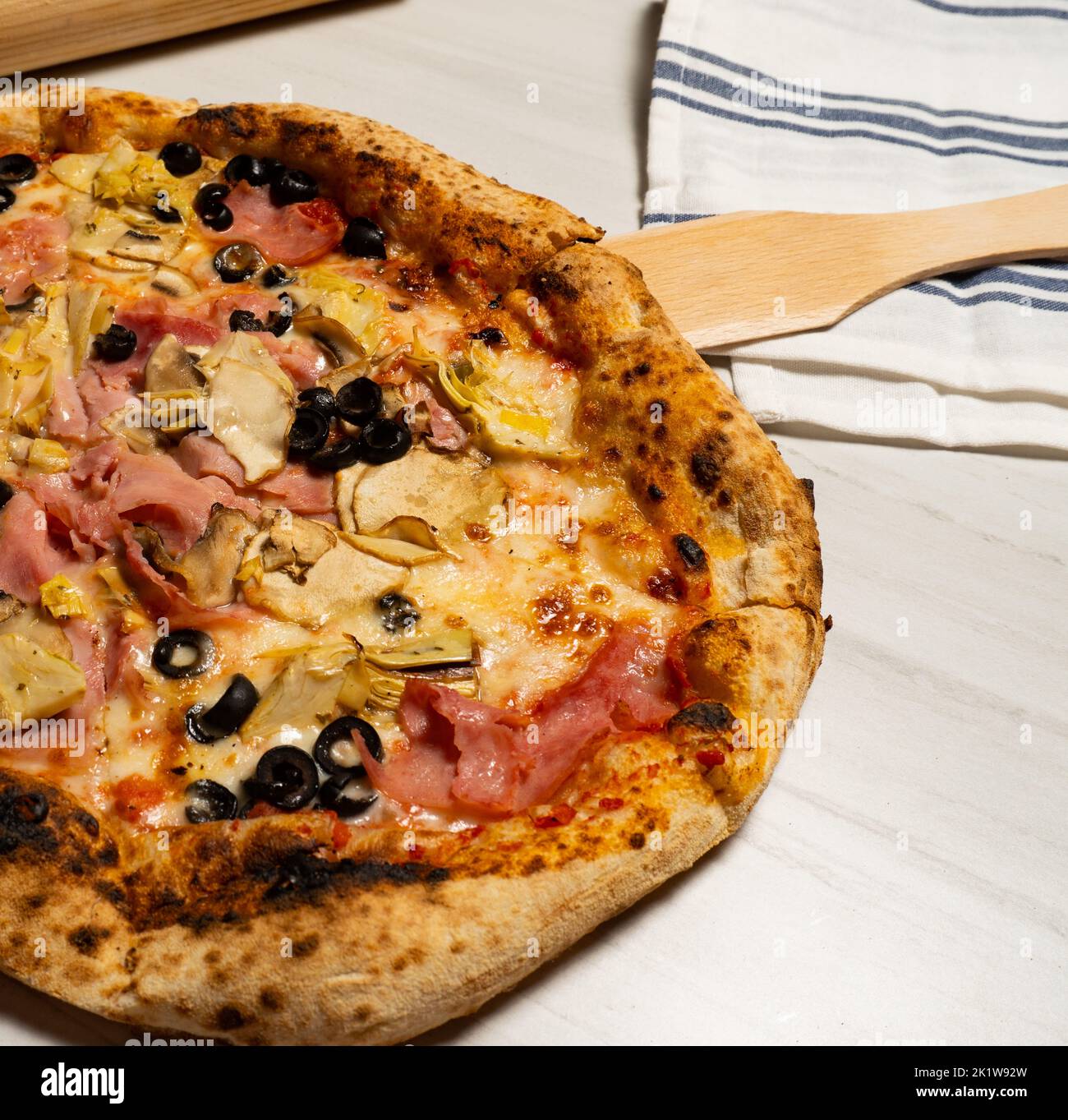 A closeup of a pizza with ham and vegetable toppings with kitchen ...