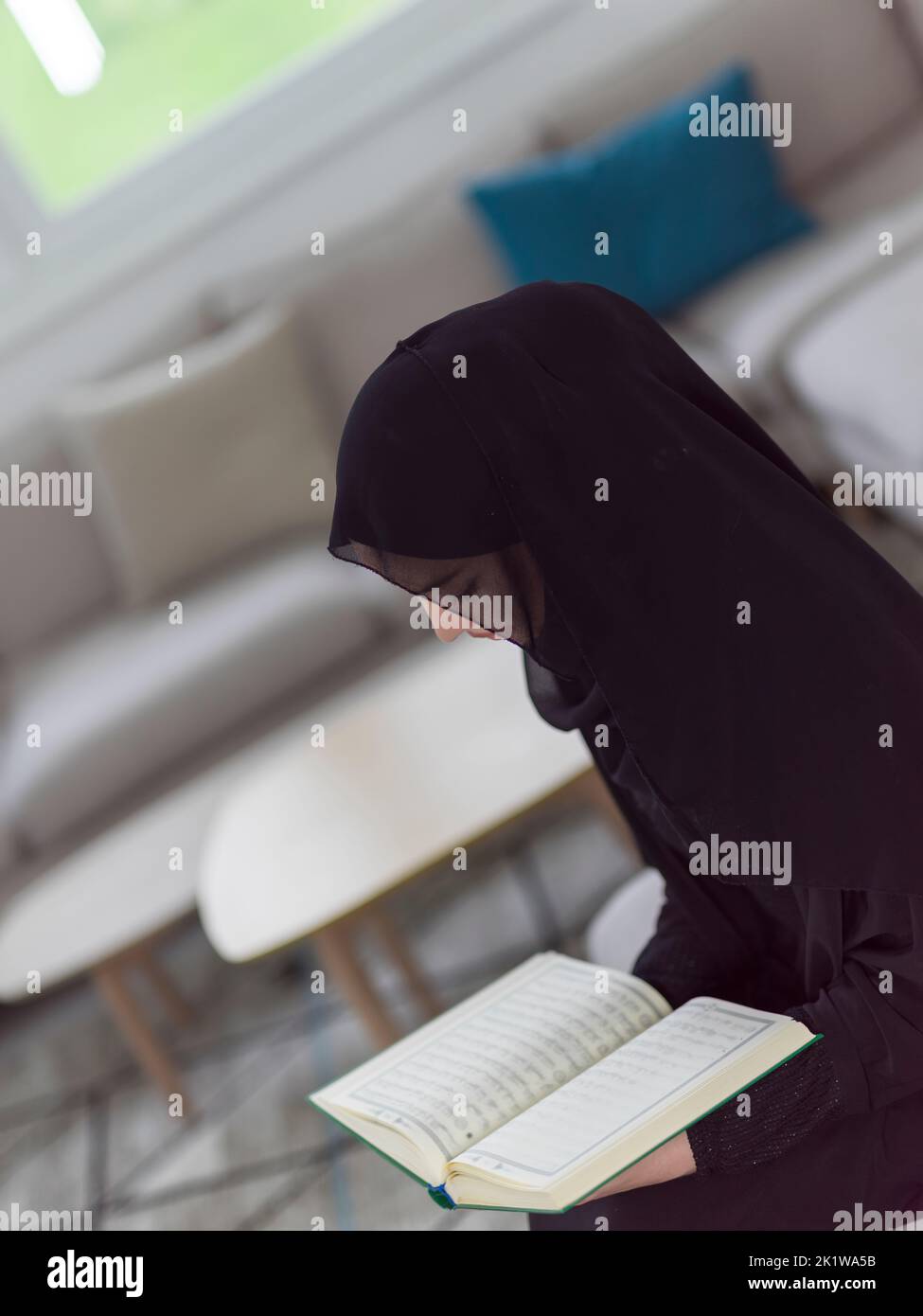 Young traditional muslim woman reading Quran on the sofa before iftar ...
