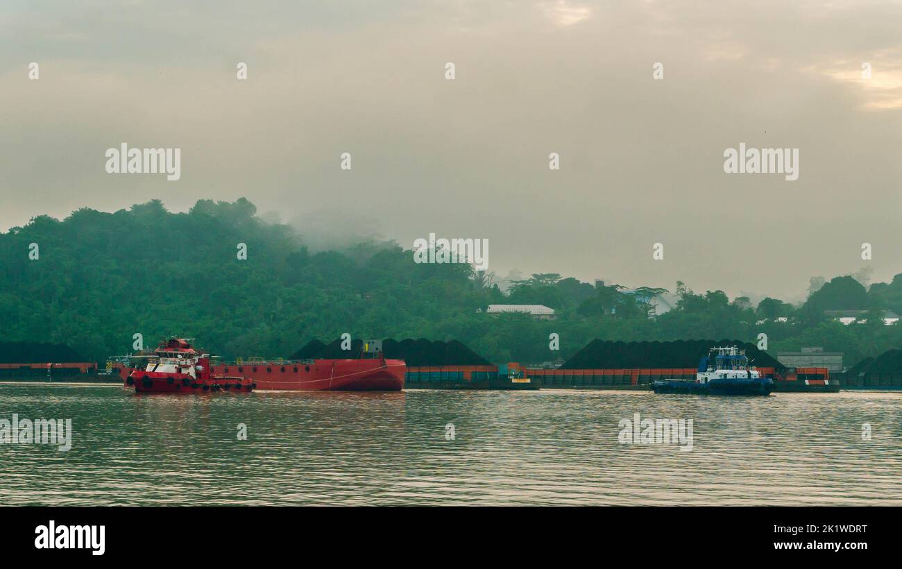 Morning traffic at Mahakam River, Samarinda. Tugboat towing huge barge ...