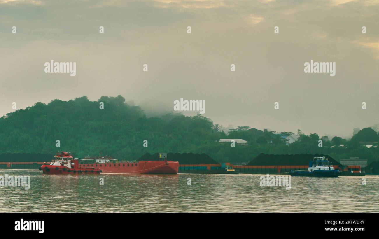 Morning traffic at Mahakam River, Samarinda. Tugboat towing huge barge ...